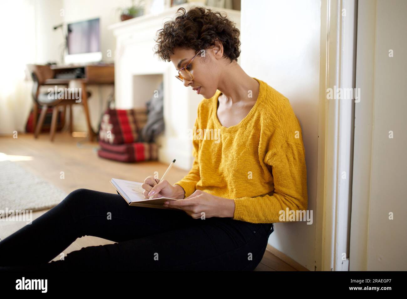 Portrait of young african american woman sitting on floor writing ideas ...