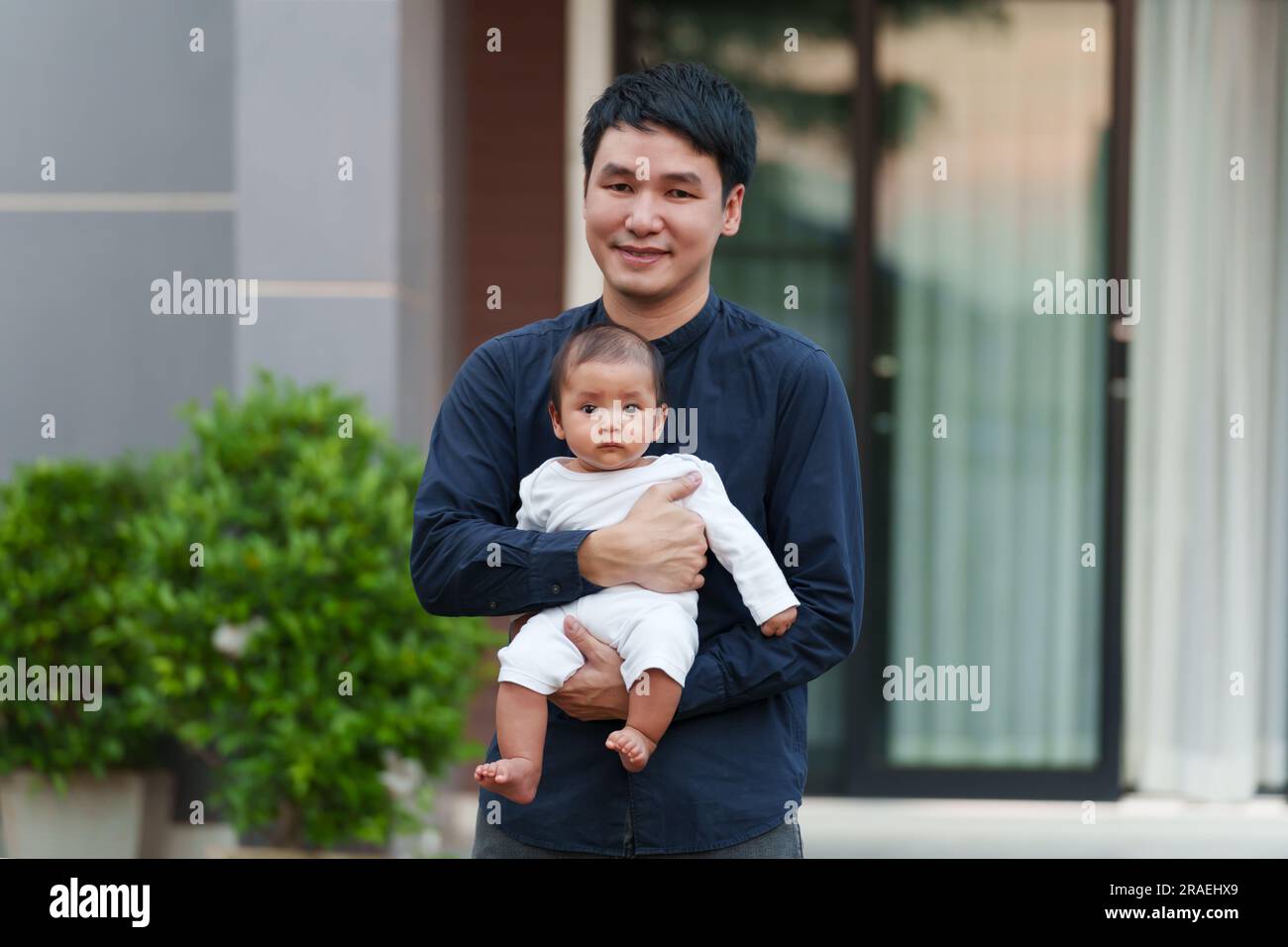 happy father holding with newborn baby while standing in front of their ...