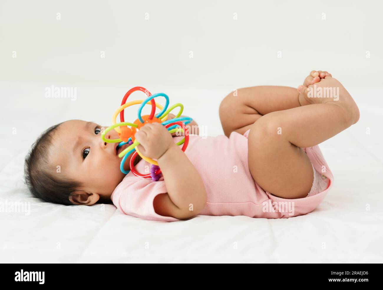 infant baby biting colorful rubber bites toy on a bed Stock Photo - Alamy