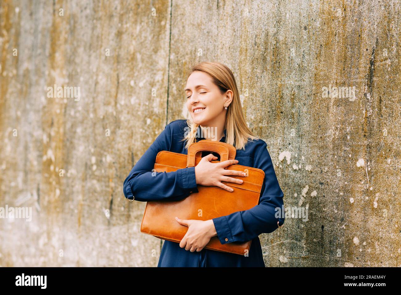 Outdoor portrait of excited woman holding brown leather briefcase ...