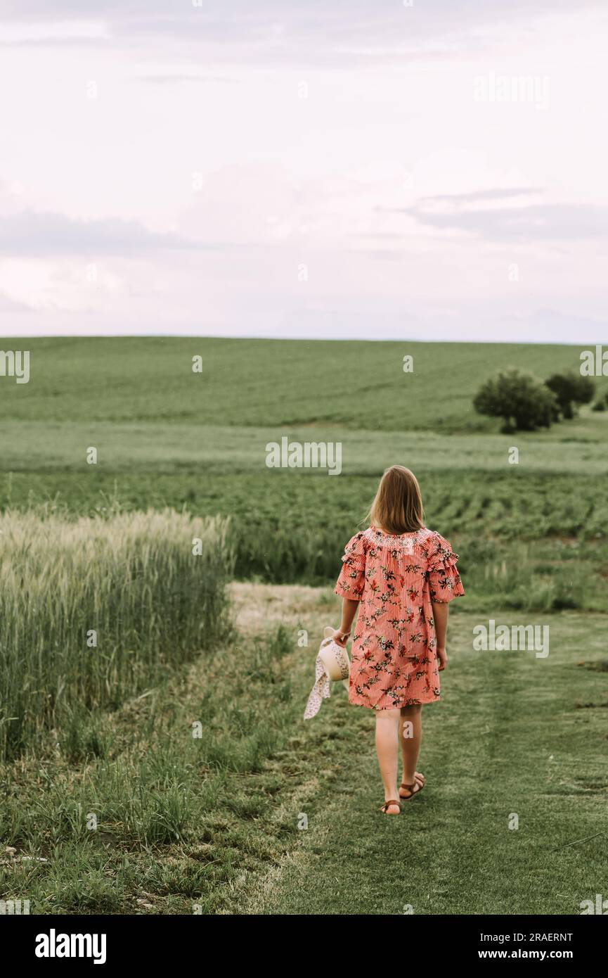Young girl walking in green fields, wearing red stripe dress, holding a ...