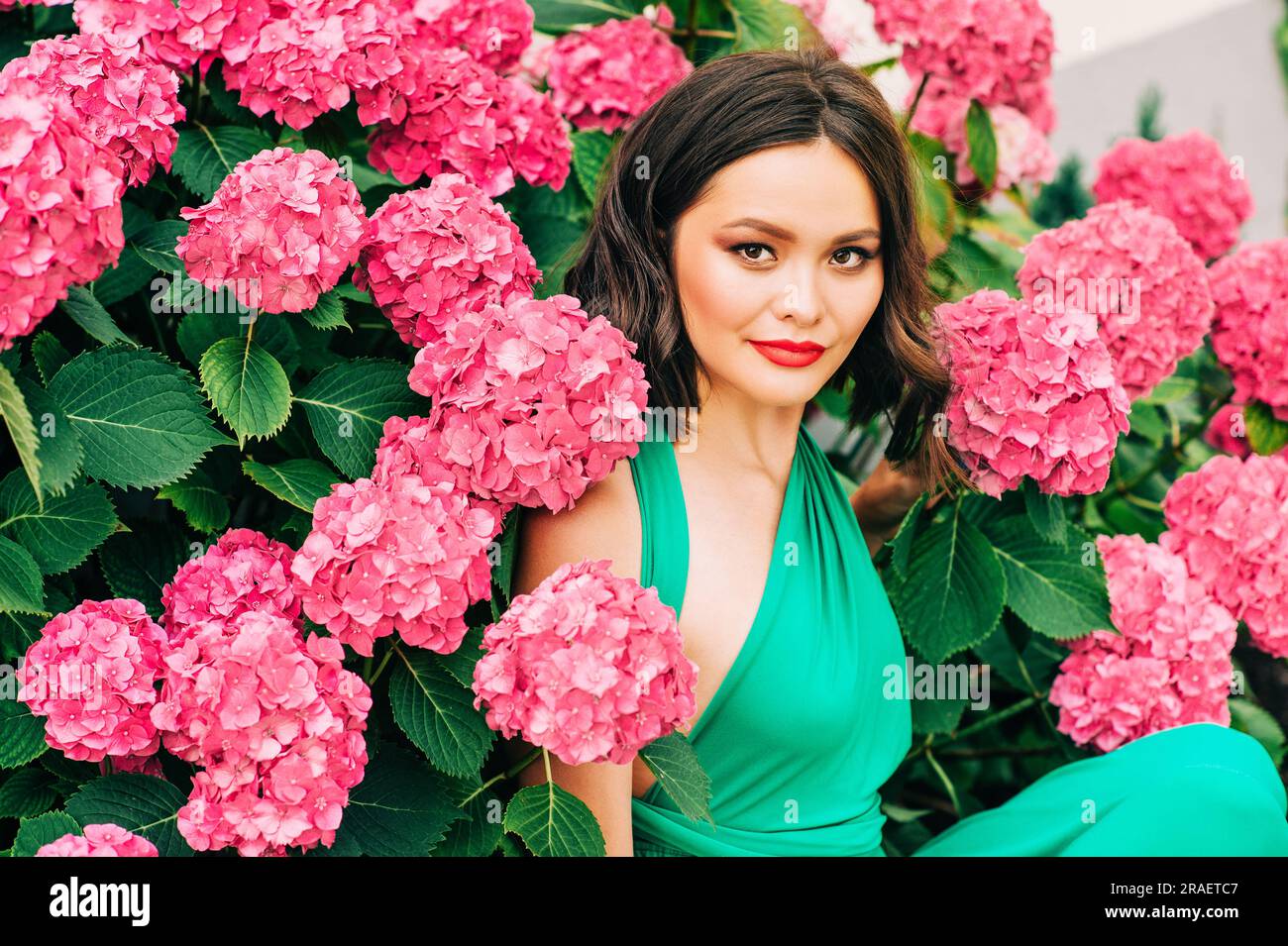 Outdoor portrait of beautiful young woman posing in pink hydrangea ...