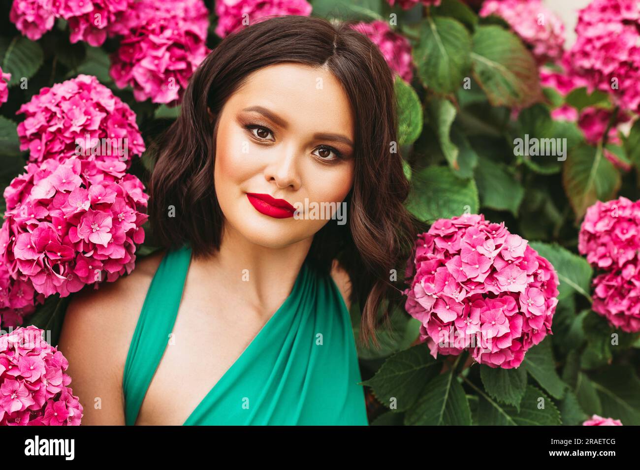 Outdoor portrait of beautiful young woman posing in pink hydrangea ...