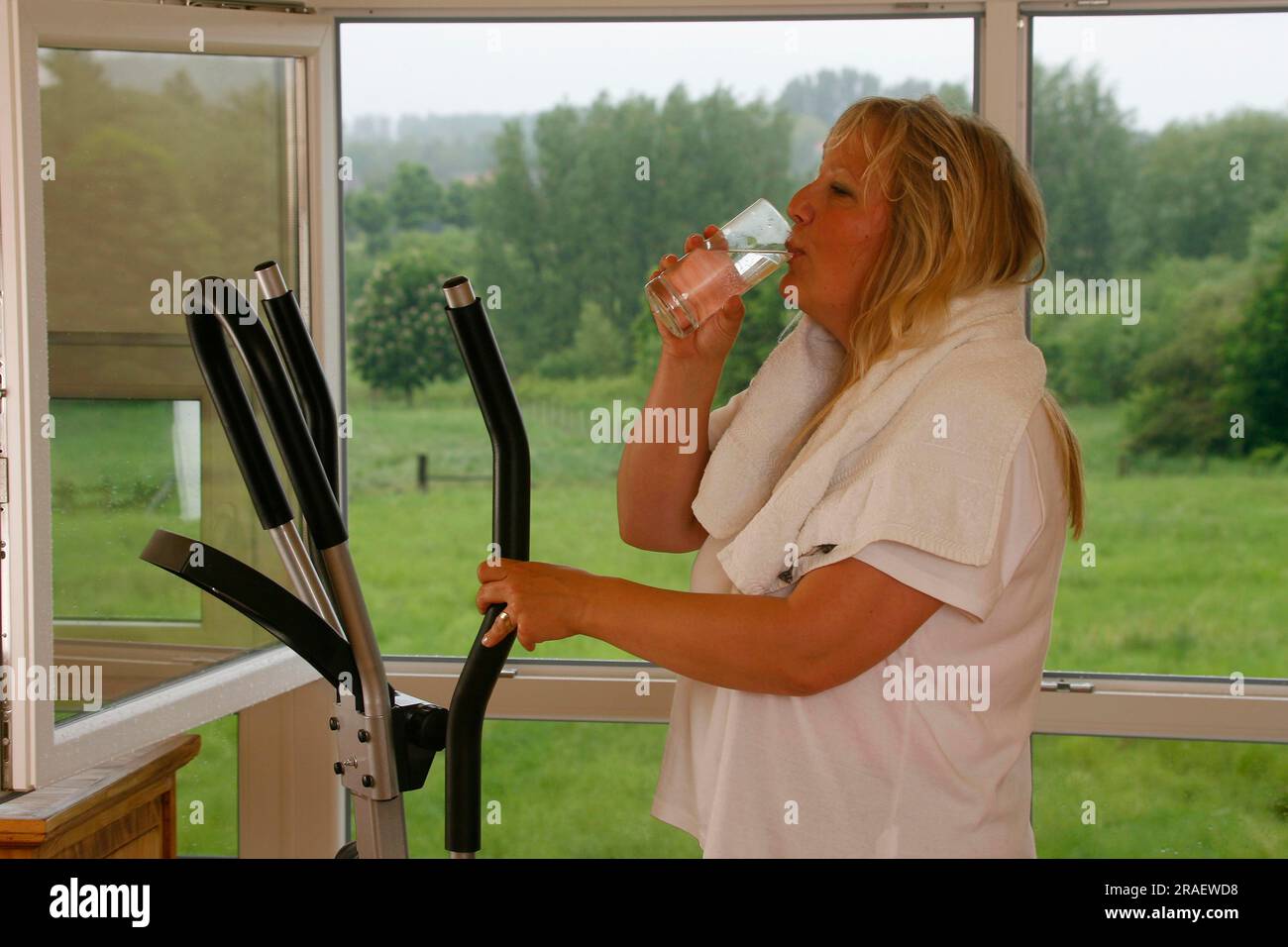 Woman on cross trainer, drinking water Stock Photo - Alamy