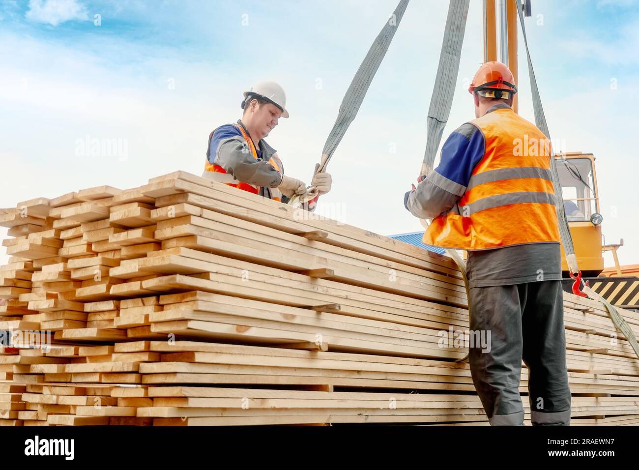 Two workers in helmets and construction vests unload wooden planks ...