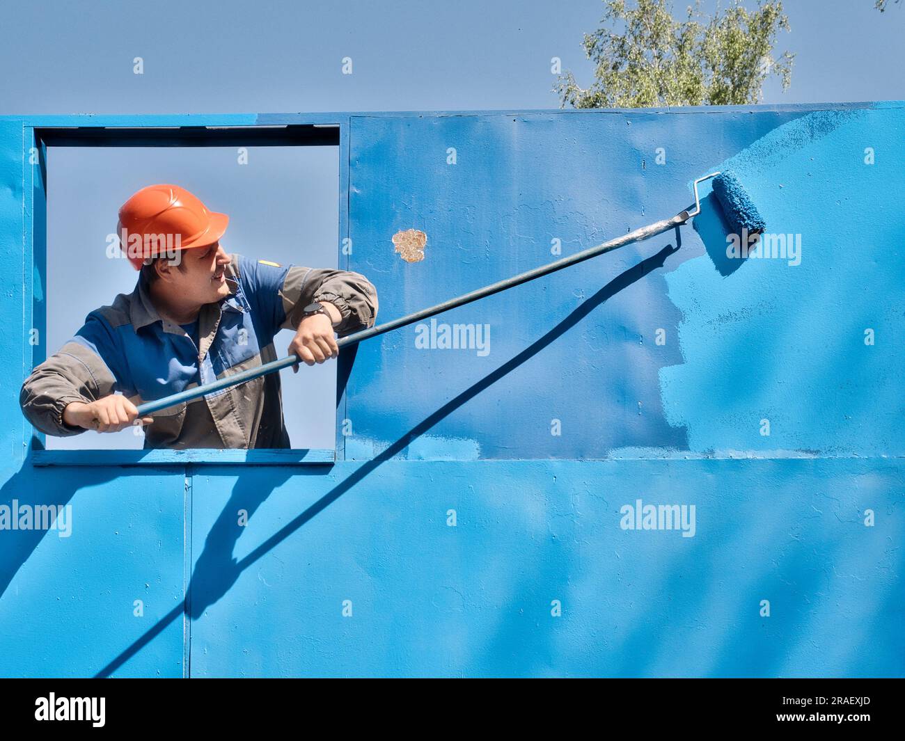 Industrial professional painter in hard hat and work clothes paints ...