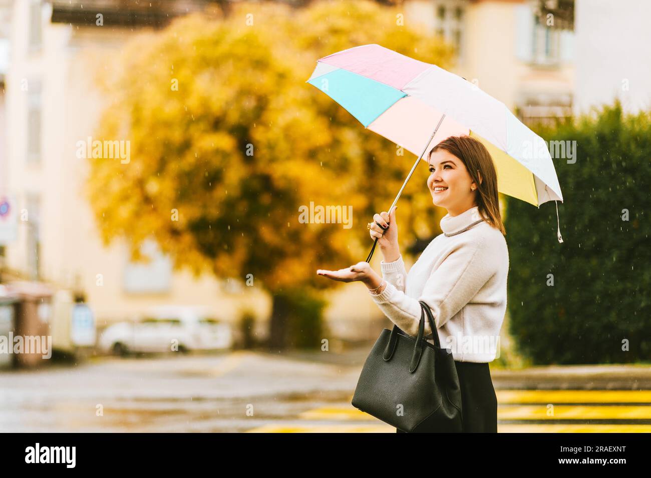 Stylish young woman under the rain, holding colorful umbrella, wearing ...
