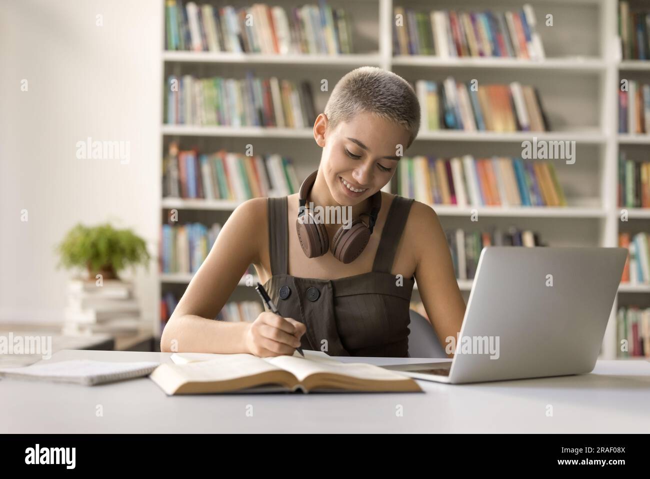 Positive student girl studying in campus library, writing notes Stock ...