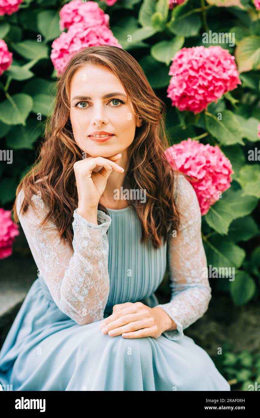 Outdoor portrait of beautiful woman posing in pink hydrangea flowers ...