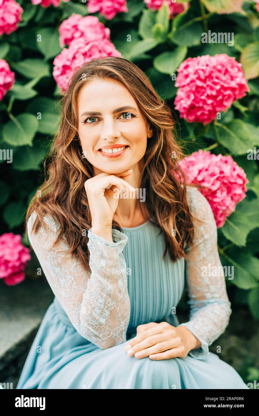 Outdoor portrait of beautiful woman posing in pink hydrangea flowers ...