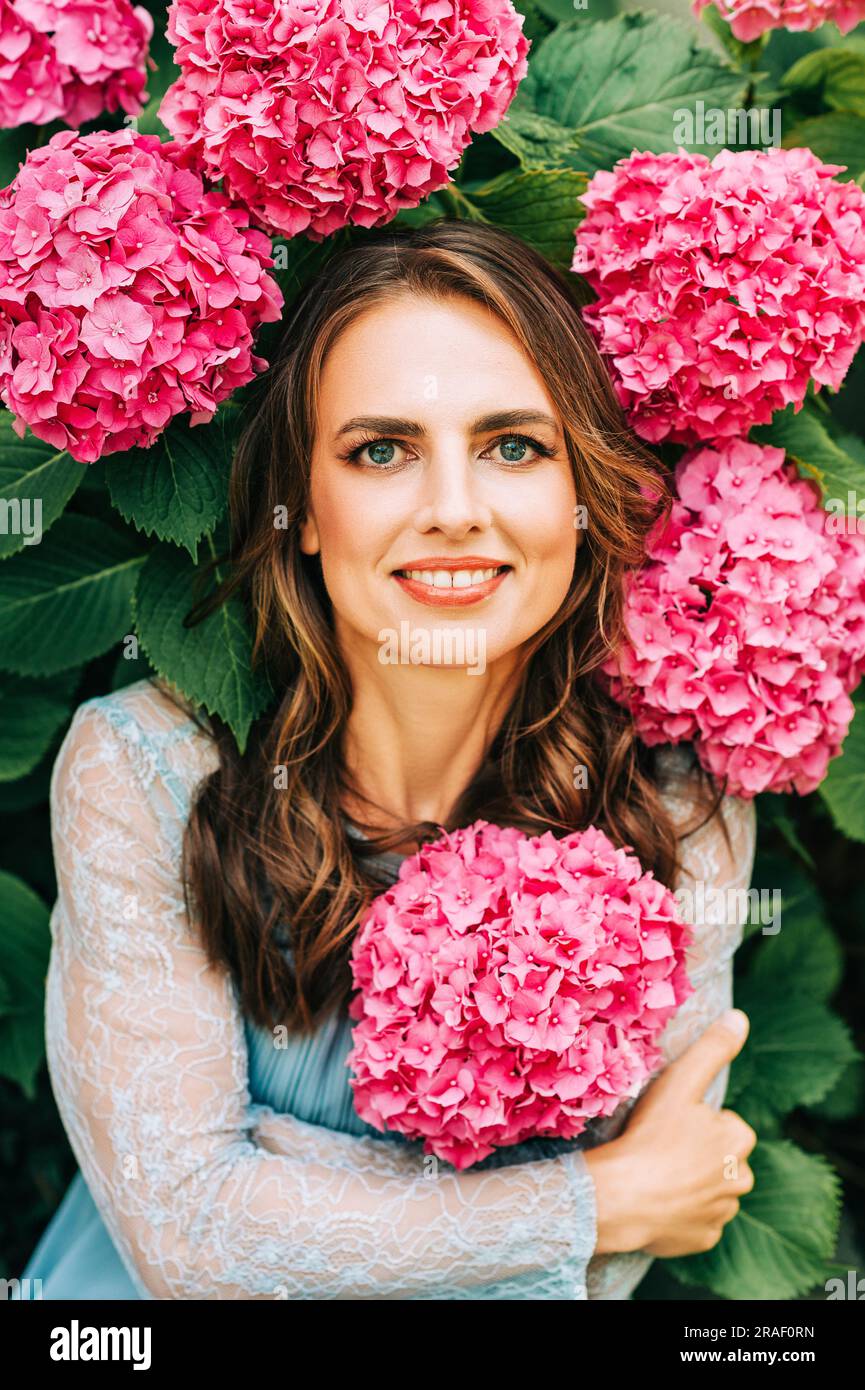 Outdoor portrait of beautiful woman posing in pink hydrangea flowers ...