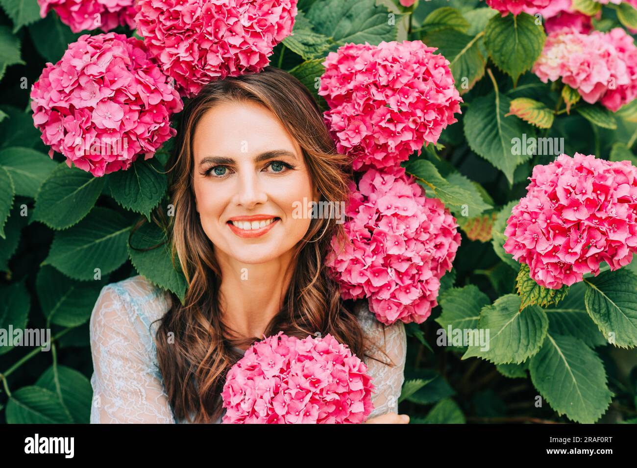 Outdoor portrait of beautiful woman posing in pink hydrangea flowers ...