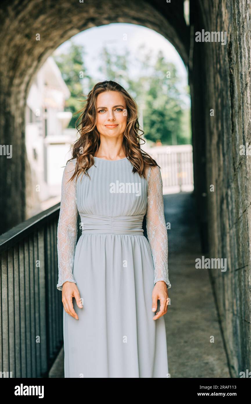 Outdoor portrait of beautiful woman with curly hair, wearing blue dress ...