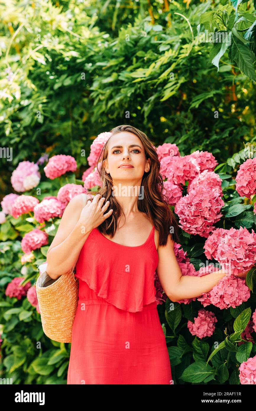 Outdoor portrait of beautiful woman posing in pink hydrangea flowers ...
