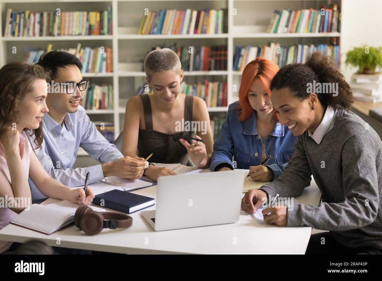 Group of positive young college students doing homework in library ...