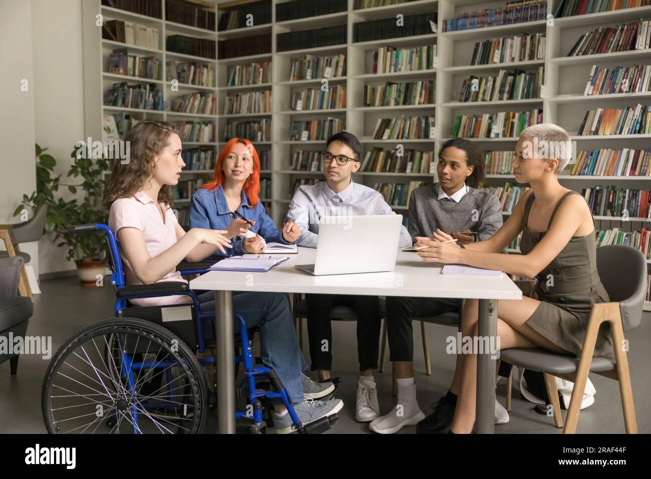 Multiethnic team of students inclusively classmate with disability ...