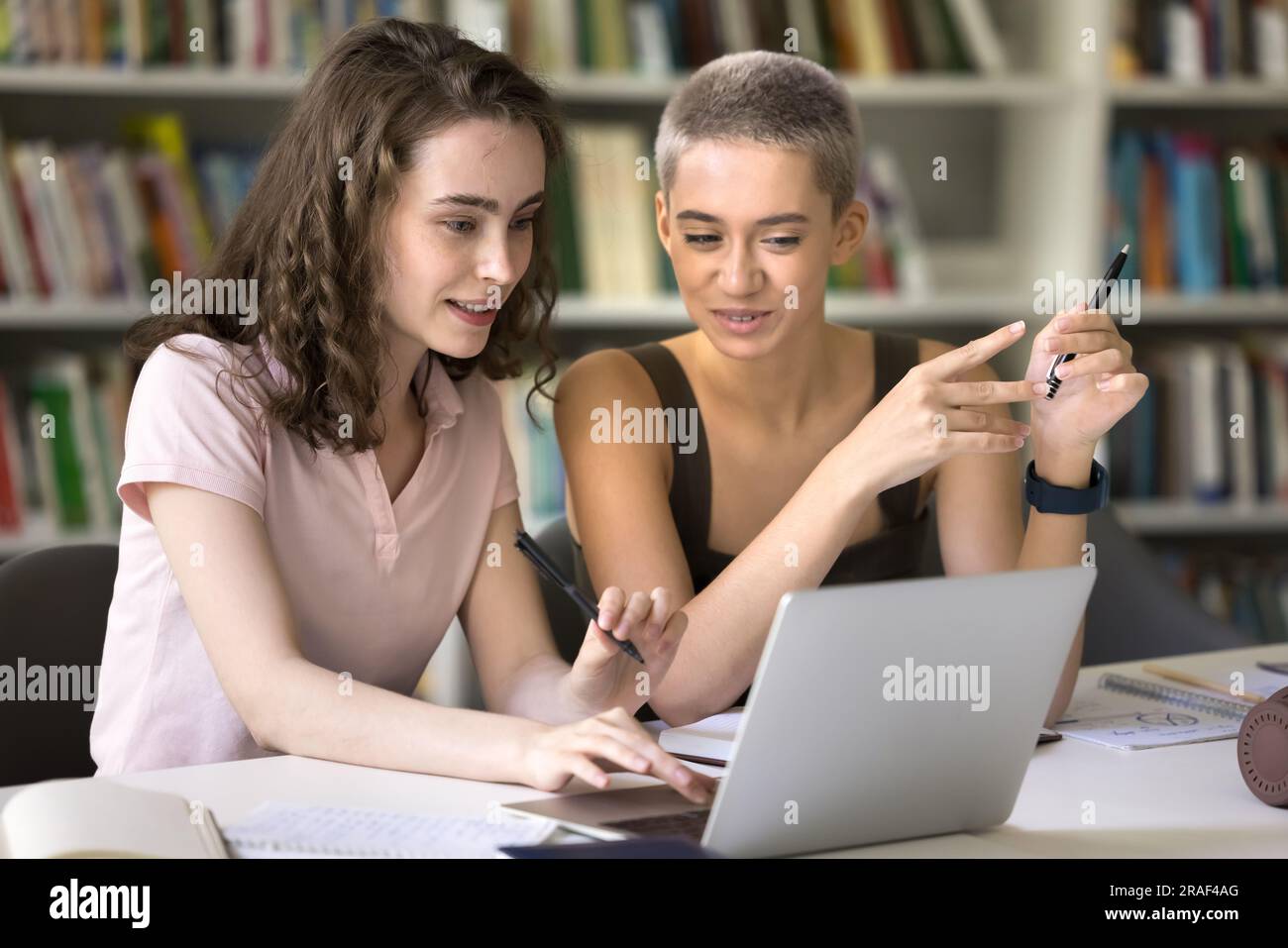 Two positive pretty young student girls studying in college library ...