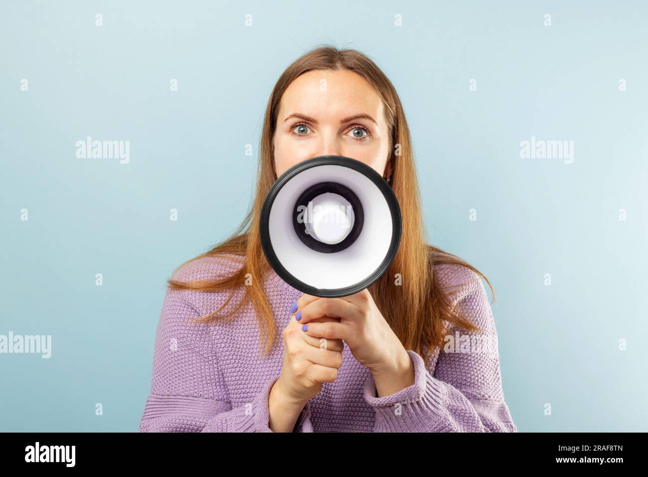 Young brunette woman shouting loudly while holding megaphone on blue ...
