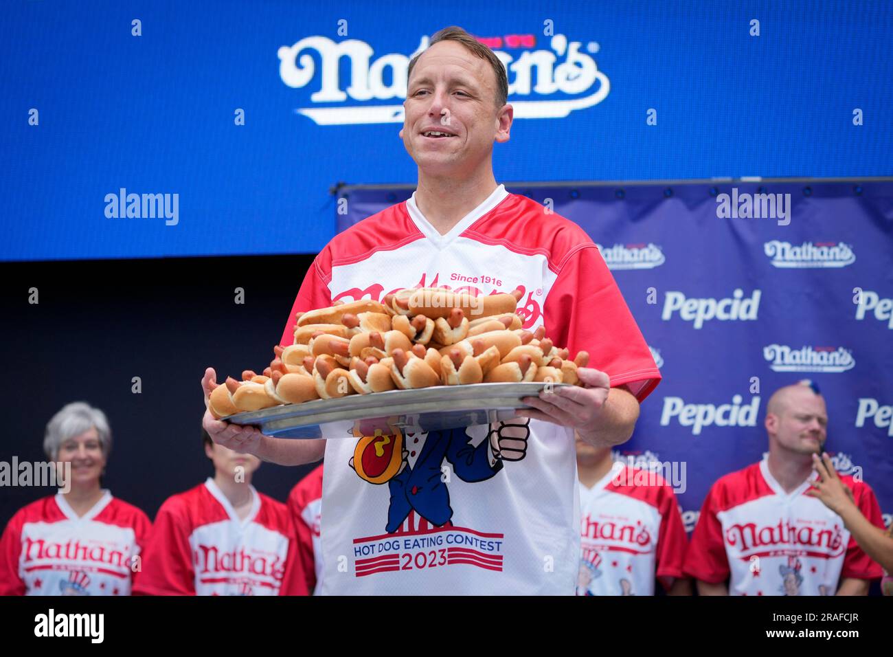 Competitive eater Joey Chestnut holds a plate of hotdogs representing ...