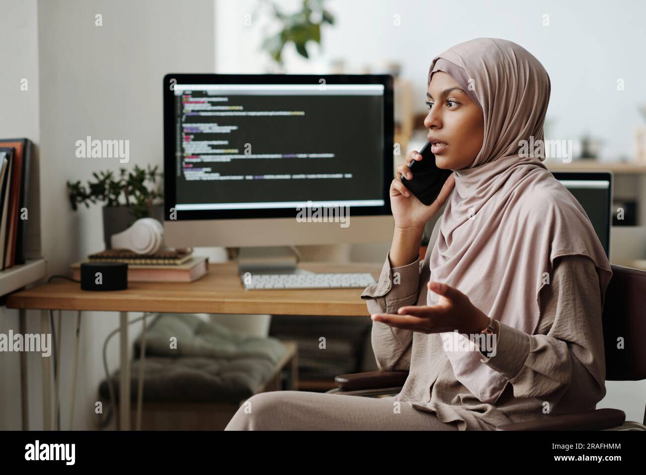 Young confident Muslim female programmer speaking on mobile phone while ...