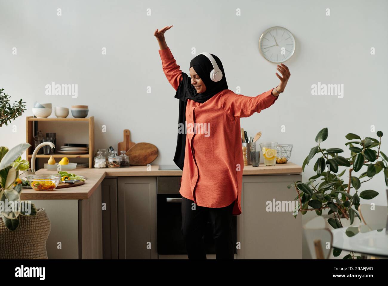 Young cheerful Muslim woman in hijab and headphones dancing in the ...