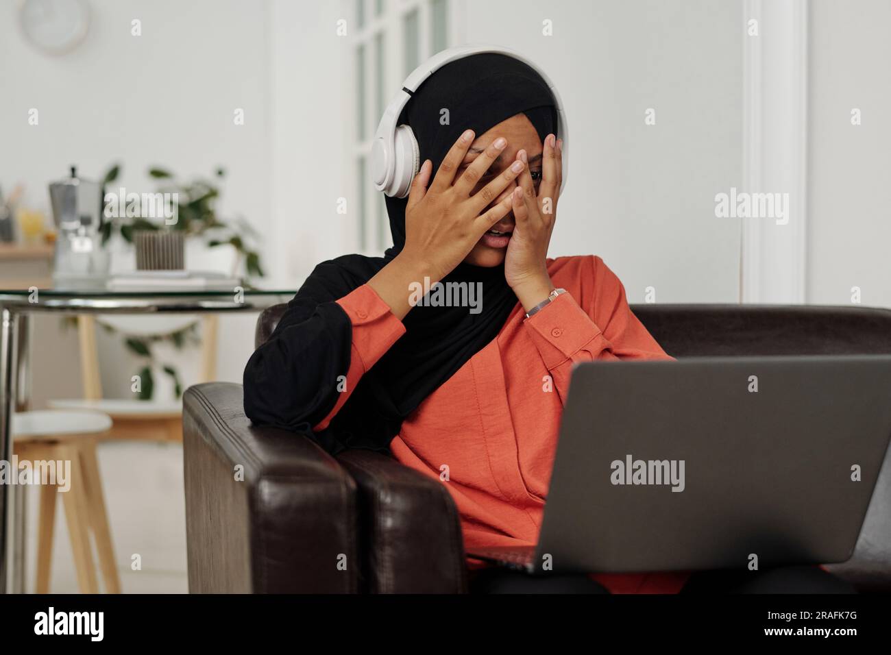 Young frightened Muslim woman with laptop on knees covering her face ...