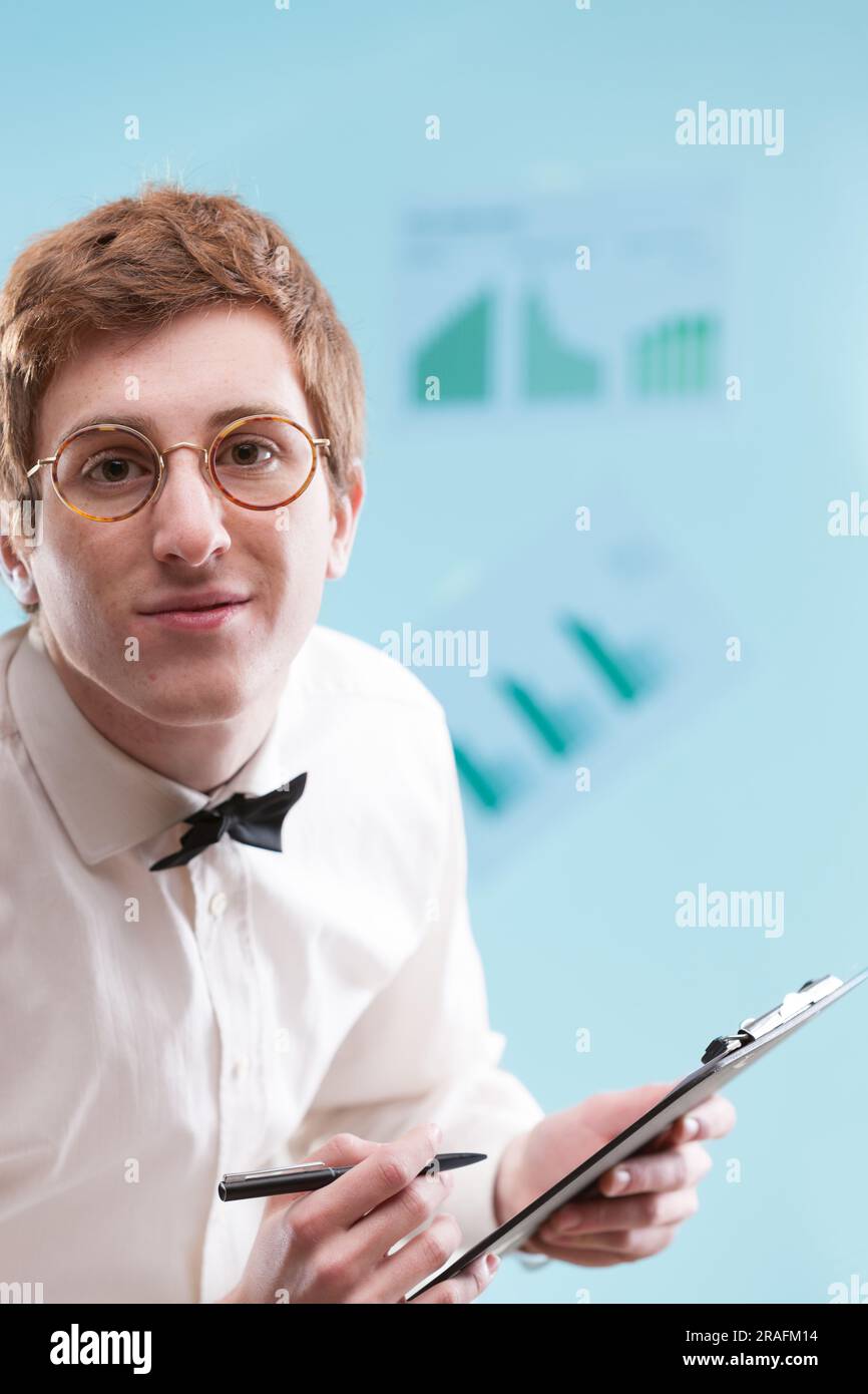 In focus, a young man with a nerdy, subservient vibe, wears a dated ...