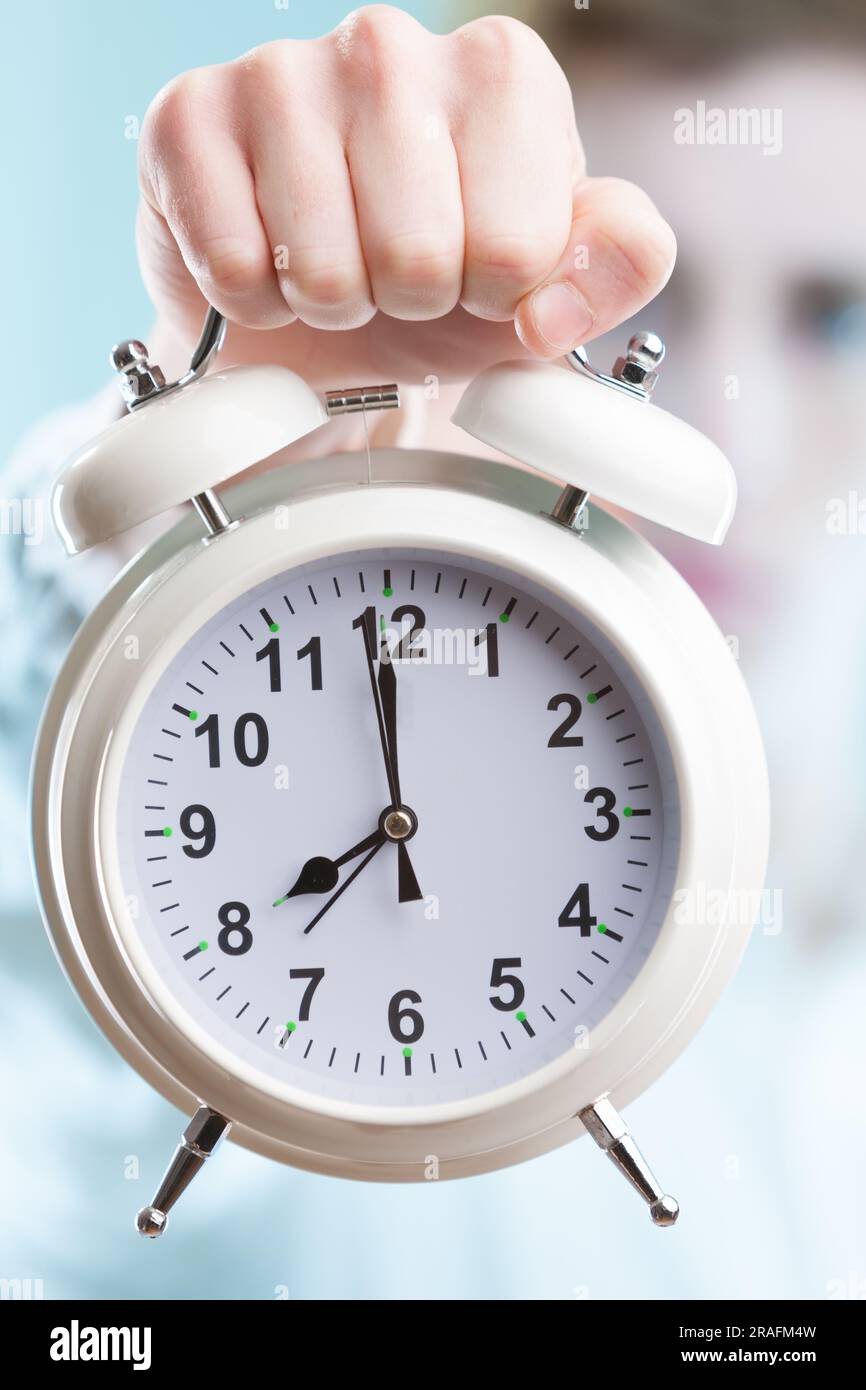 An in-focus hand extending a large alarm clock against a blurry office ...