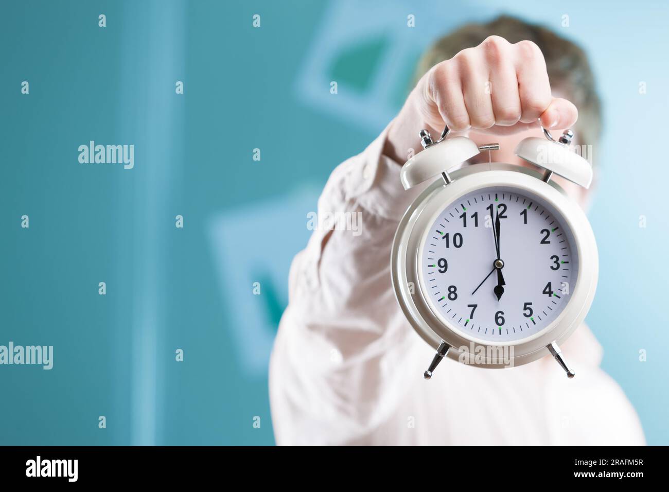 Against a blurry office backdrop, a hand extends a sizable clock. In ...