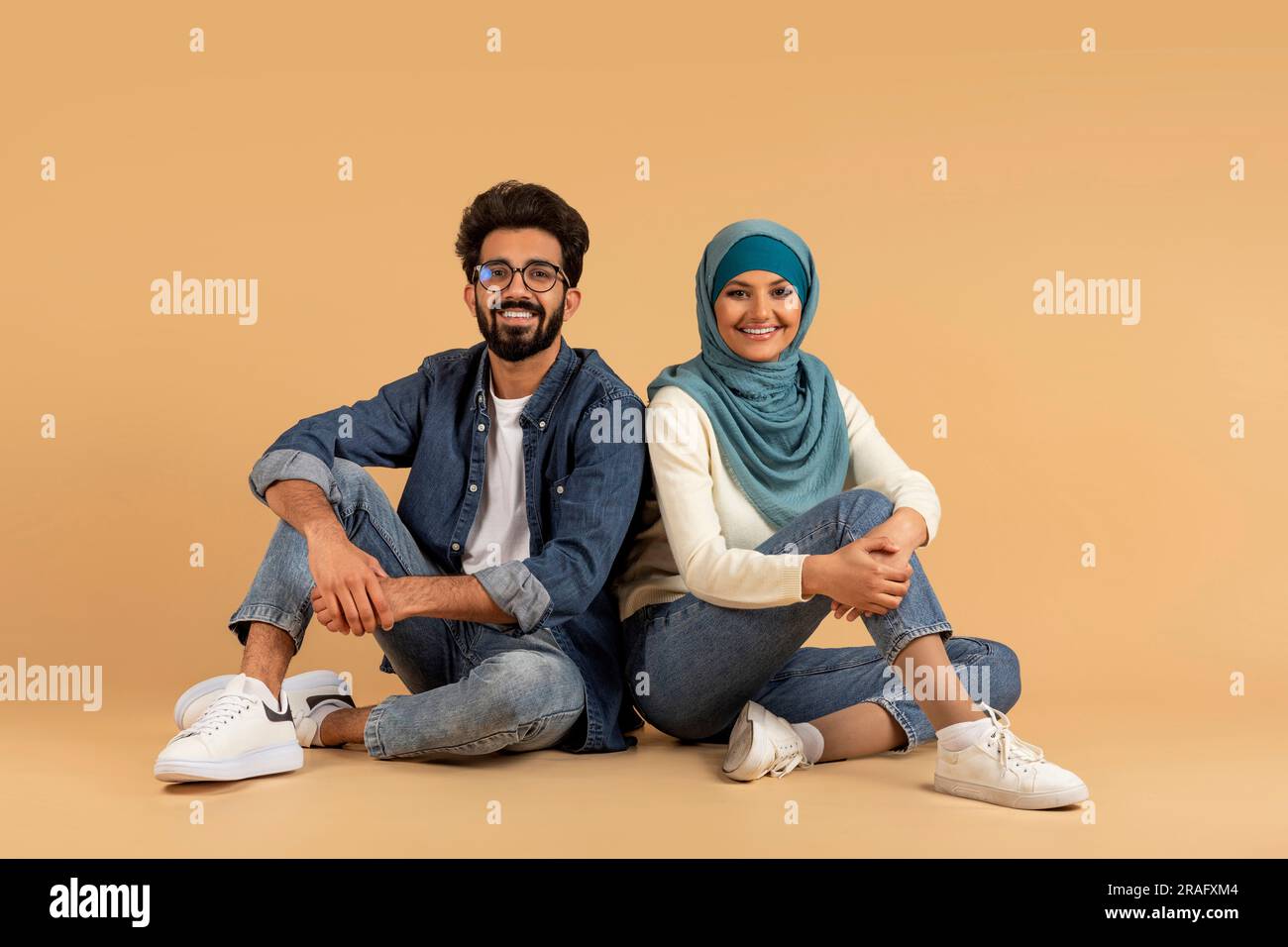 Happy Arabic Man And Woman In Hijab Sitting Over Beige Studio ...