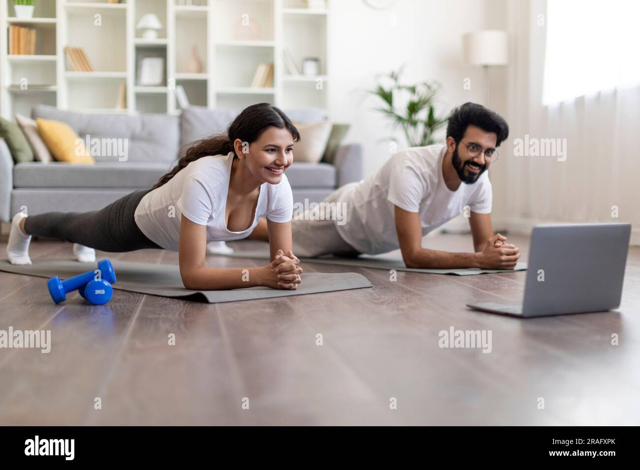 Training At Home. Sporty indian couple doing plank exercise with laptop ...