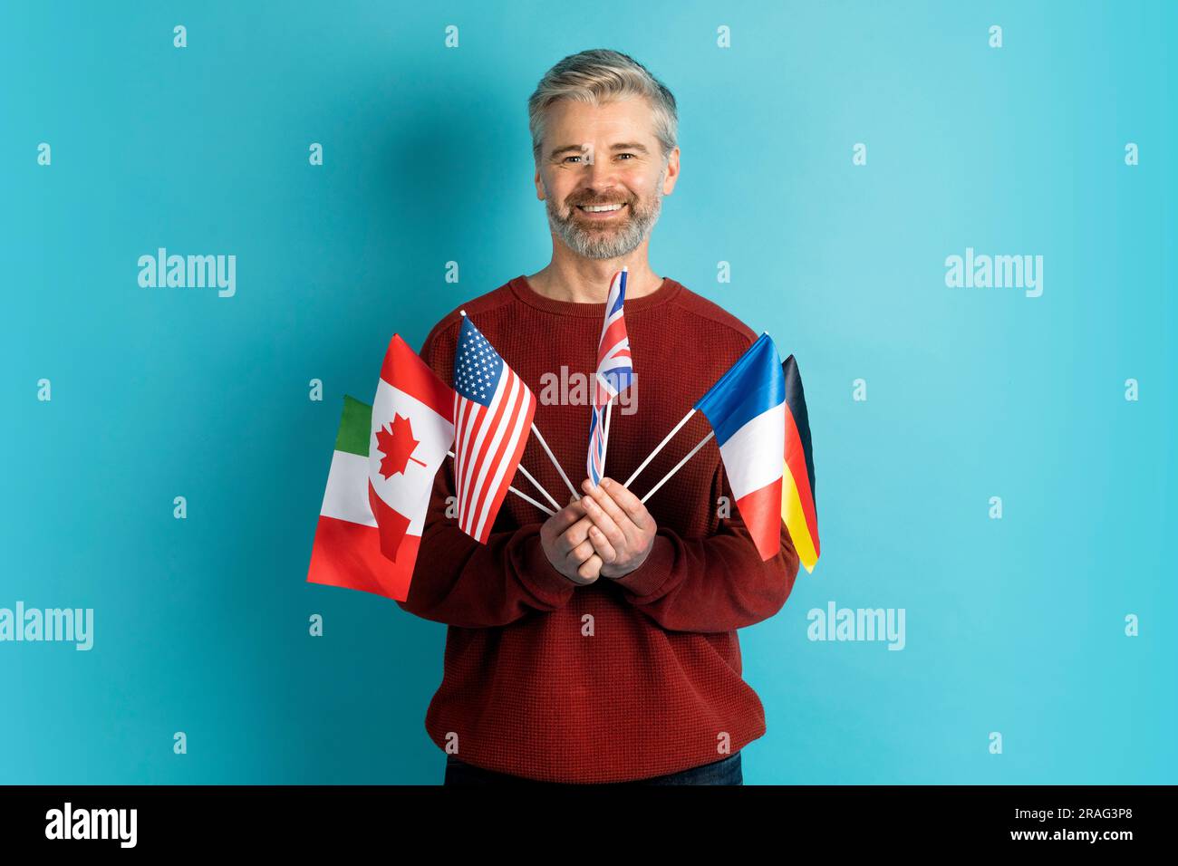Cheerful grey-haired mature man holding flags of different countries ...