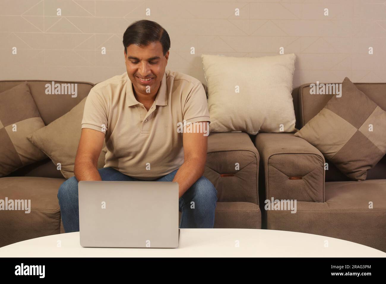 happy Indian man working from home on a laptop sitting on a couch Stock ...