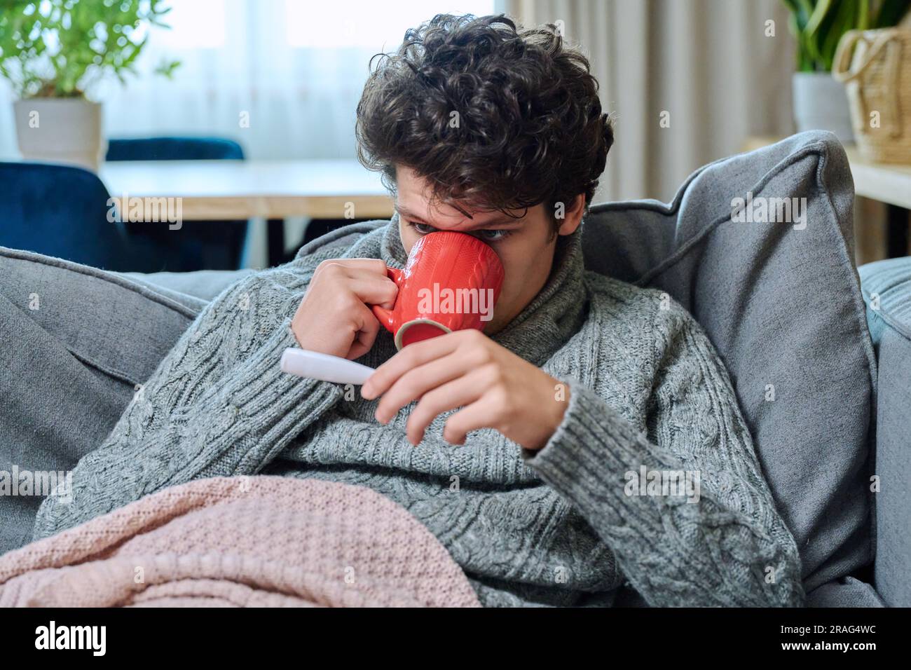 Young guy checking temperature, lying on couch under blanket Stock ...