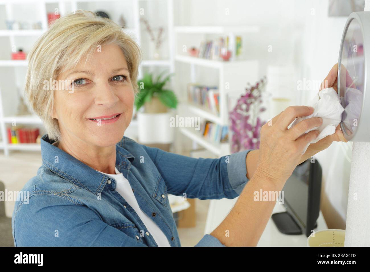 mature woman dusting clock in her home Stock Photo - Alamy