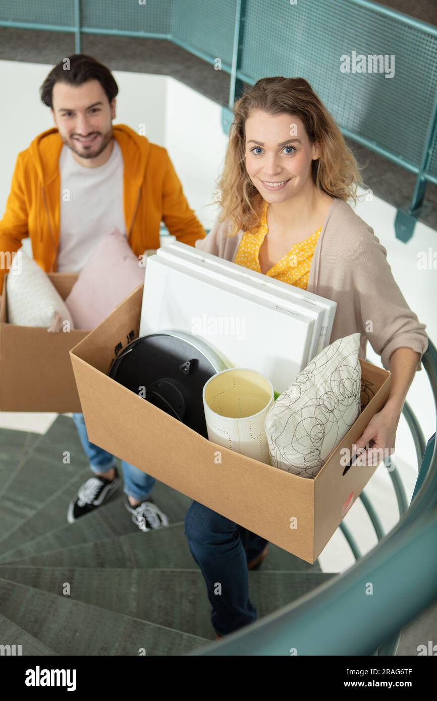 happy young couple holding cardboard boxes while climbing the stairs ...
