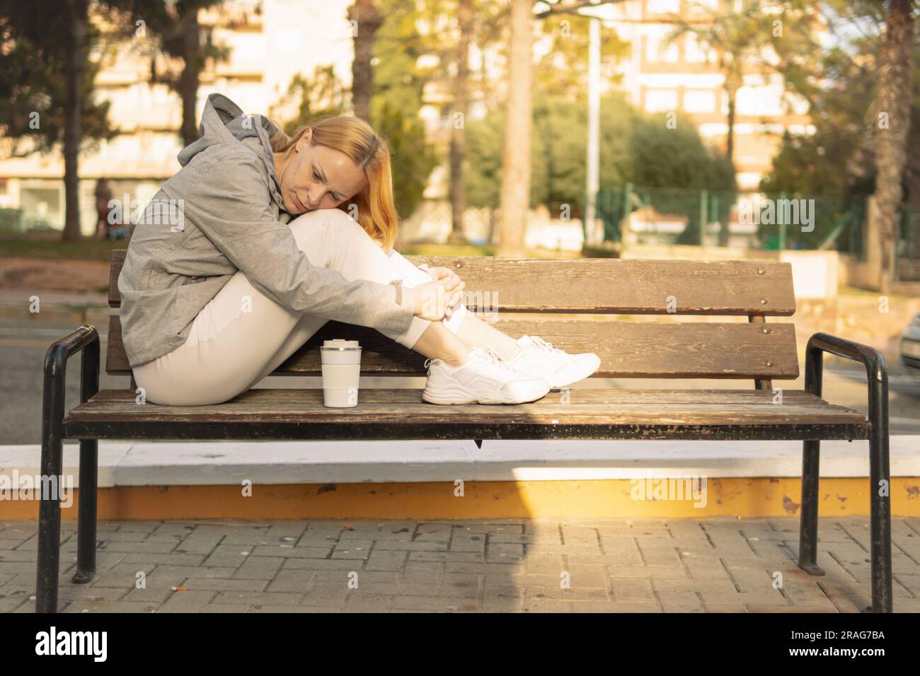 sad girl is sitting on bench with her feet and lowered head to her feet ...