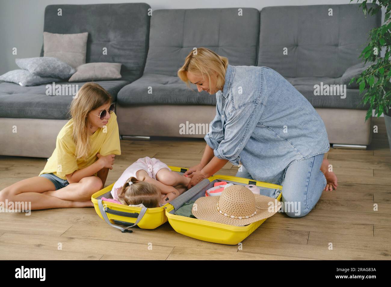 Mother with daughters packing yellow suitcase for travel. Family having fun going on vacation ...