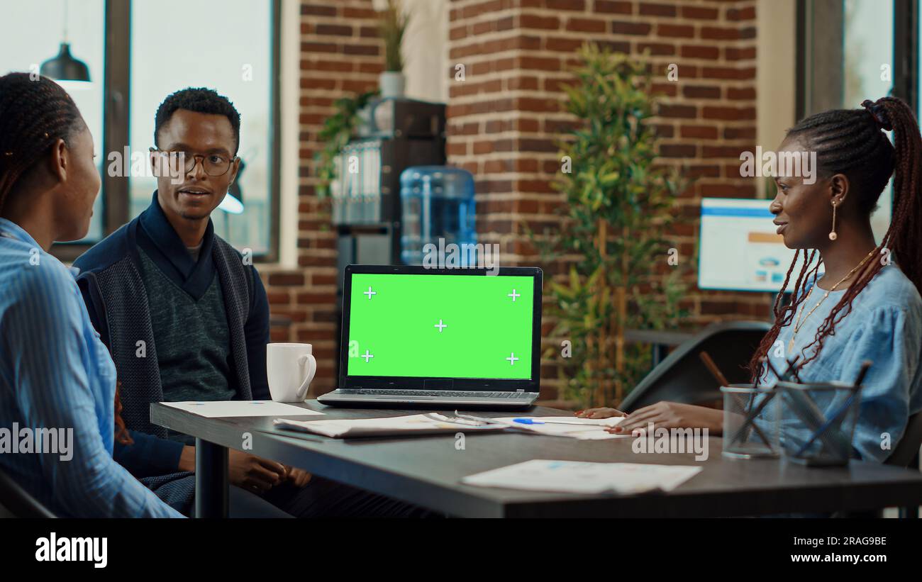 Colleagues looking at greenscreen laptop in briefing meeting, working ...