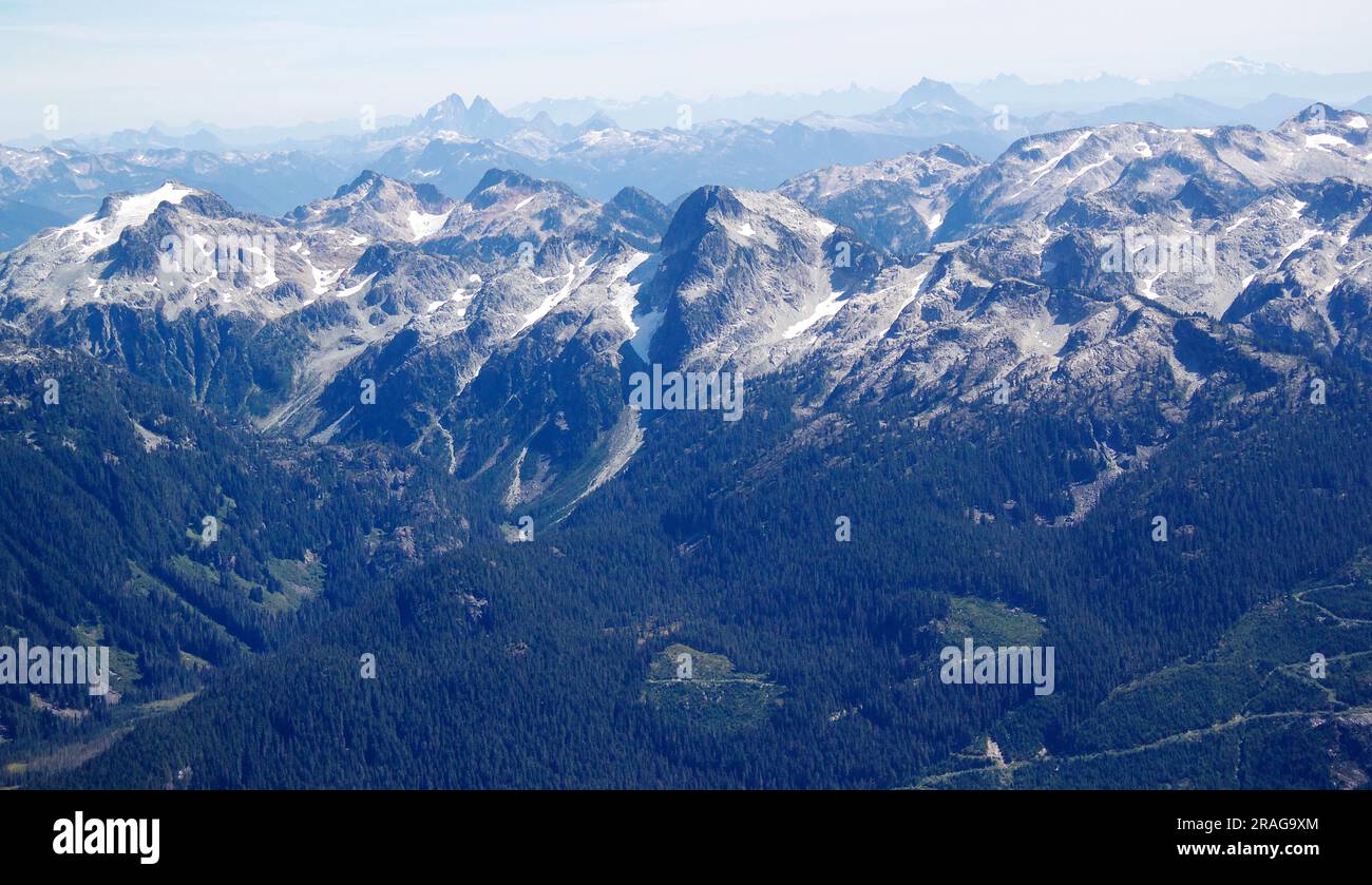Peaks of mountains are surrounded by evergreen trees. In British ...