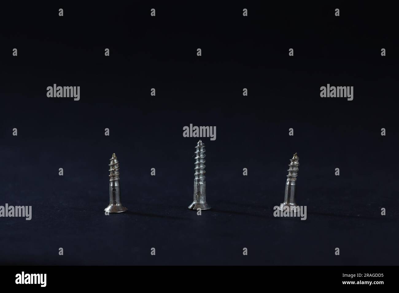 Picture of three screws isolated on a black background, silver white ...