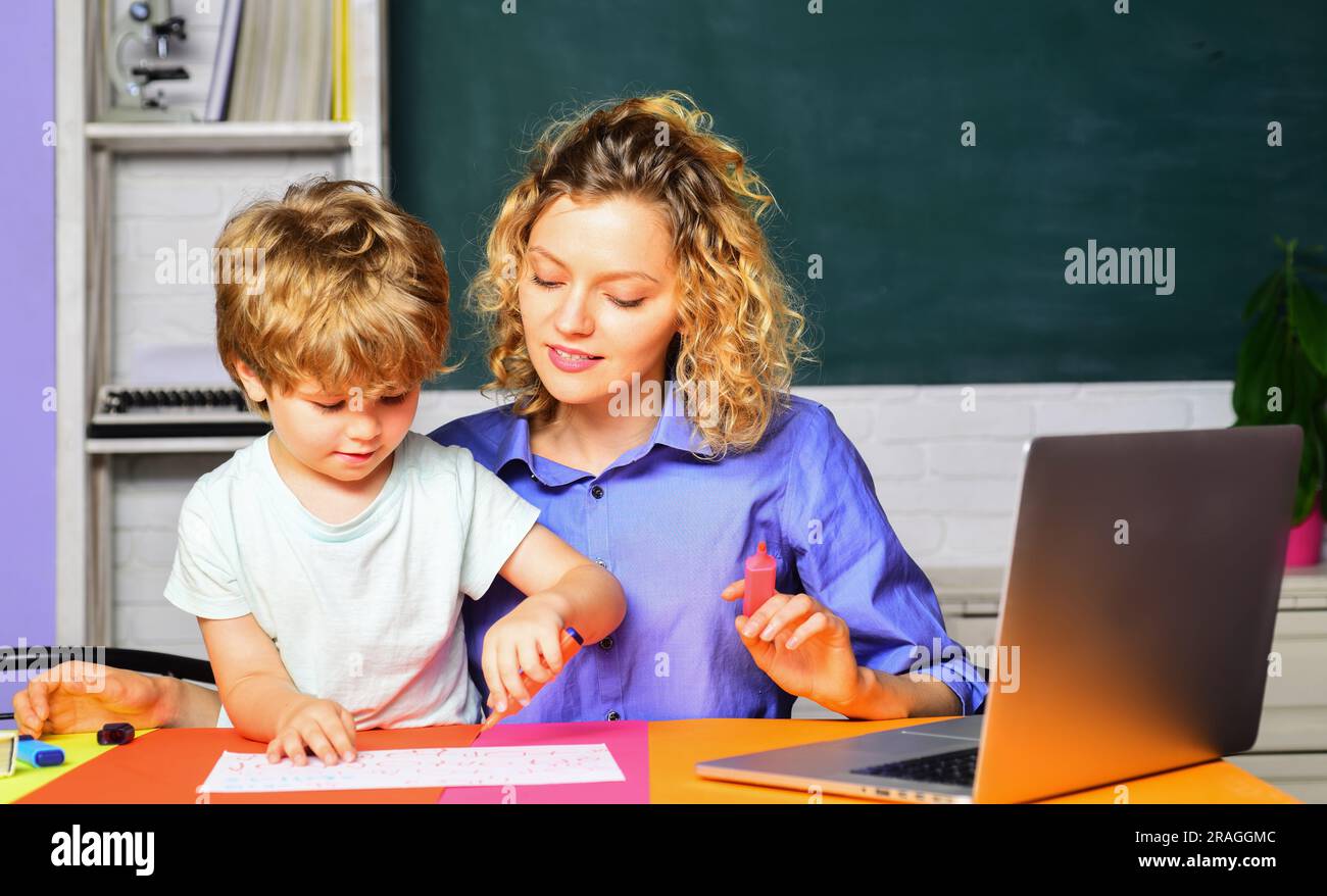 Female elementary school teacher helping little boy with writing lesson ...