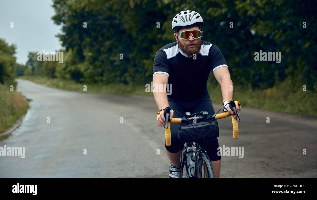 Young bearded man, cyclist in helmet, glasses and uniform riding bike ...
