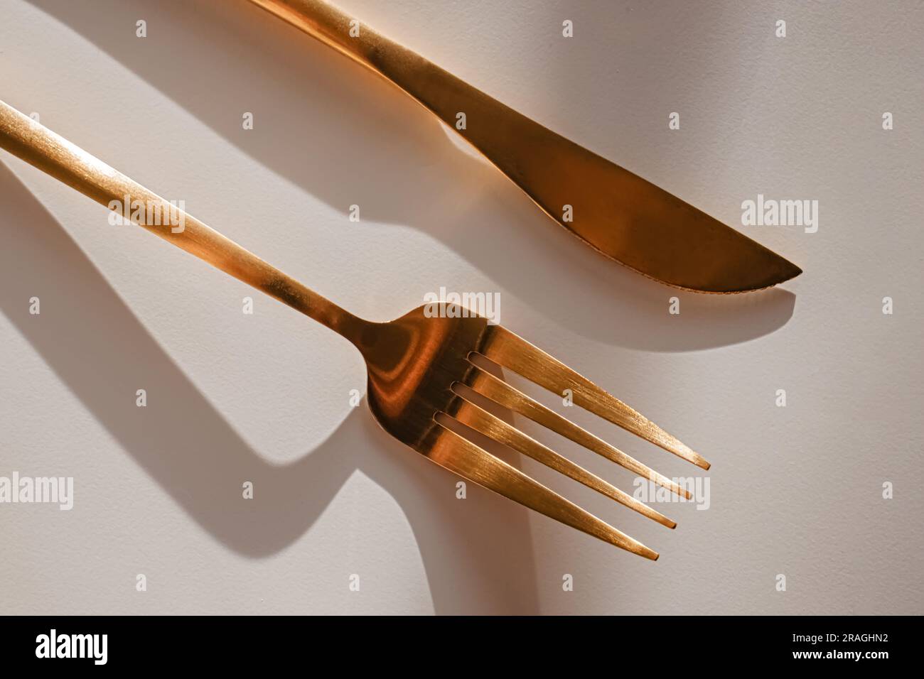 Golden knife and fork on the white table in natural light with long ...