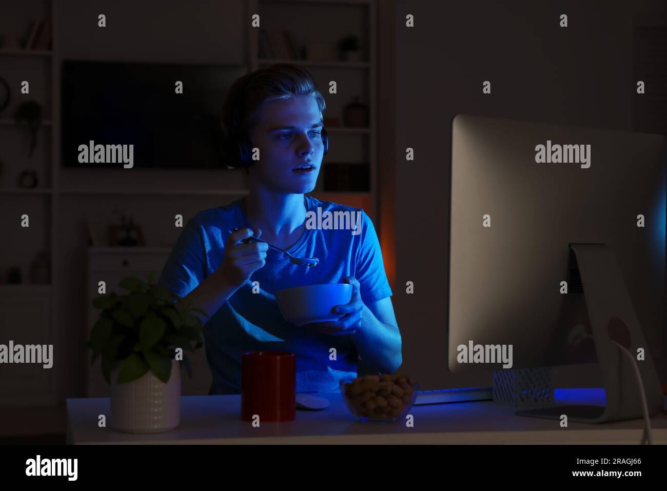 Teenage boy eating porridge while using computer in room at night ...