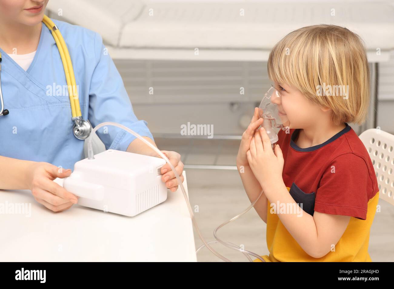 Medical assistant sitting near sick little boy while he using nebulizer ...