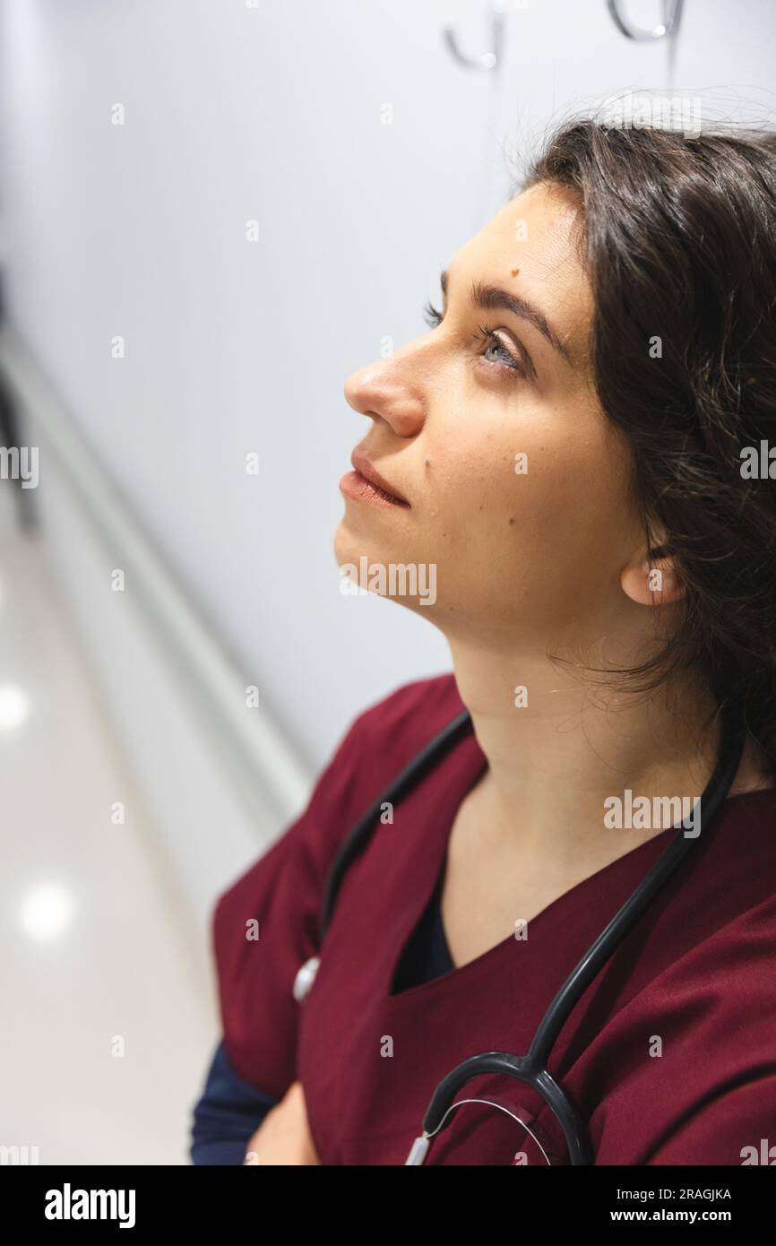 Tired caucasian female doctor wearing scrubs, leaning on wall in ...