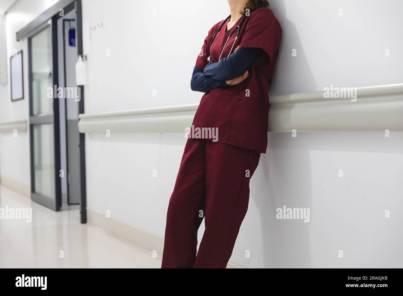 Midsection of caucasian female doctor wearing scrubs, leaning on wall ...
