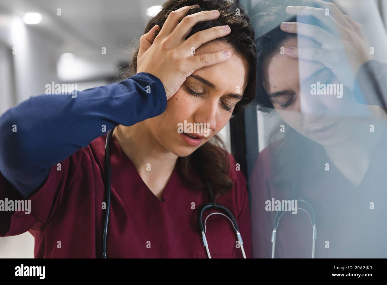 Tired caucasian female doctor wearing scrubs, leaning on wall in ...