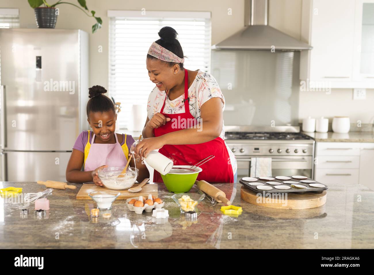 Happy african american mother and daughter baking cookies, adding ...